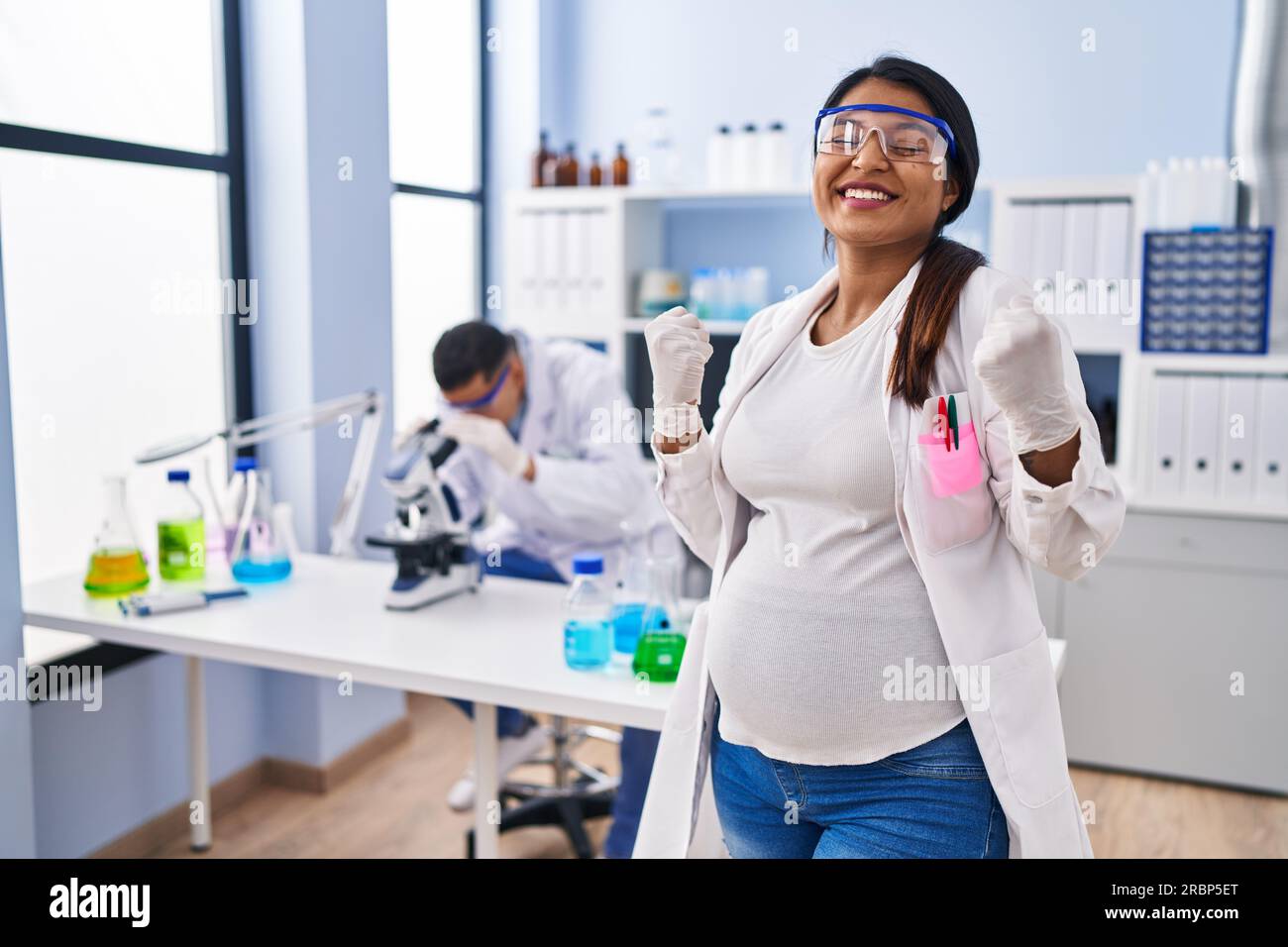 Young hispanic woman expecting a baby working at scientist laboratory ...