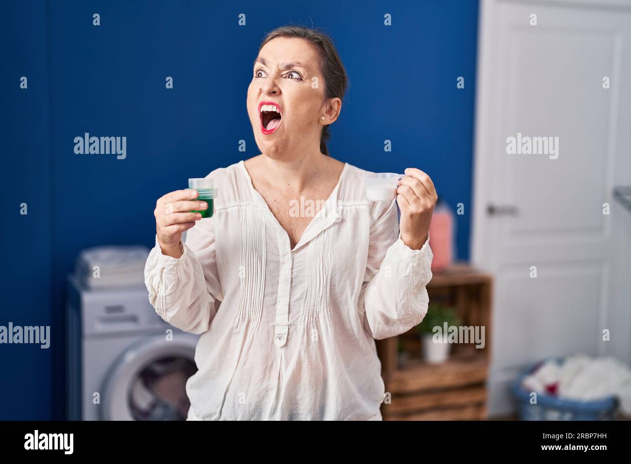 Middle age hispanic woman holding laundry detergent and laundry powder ...