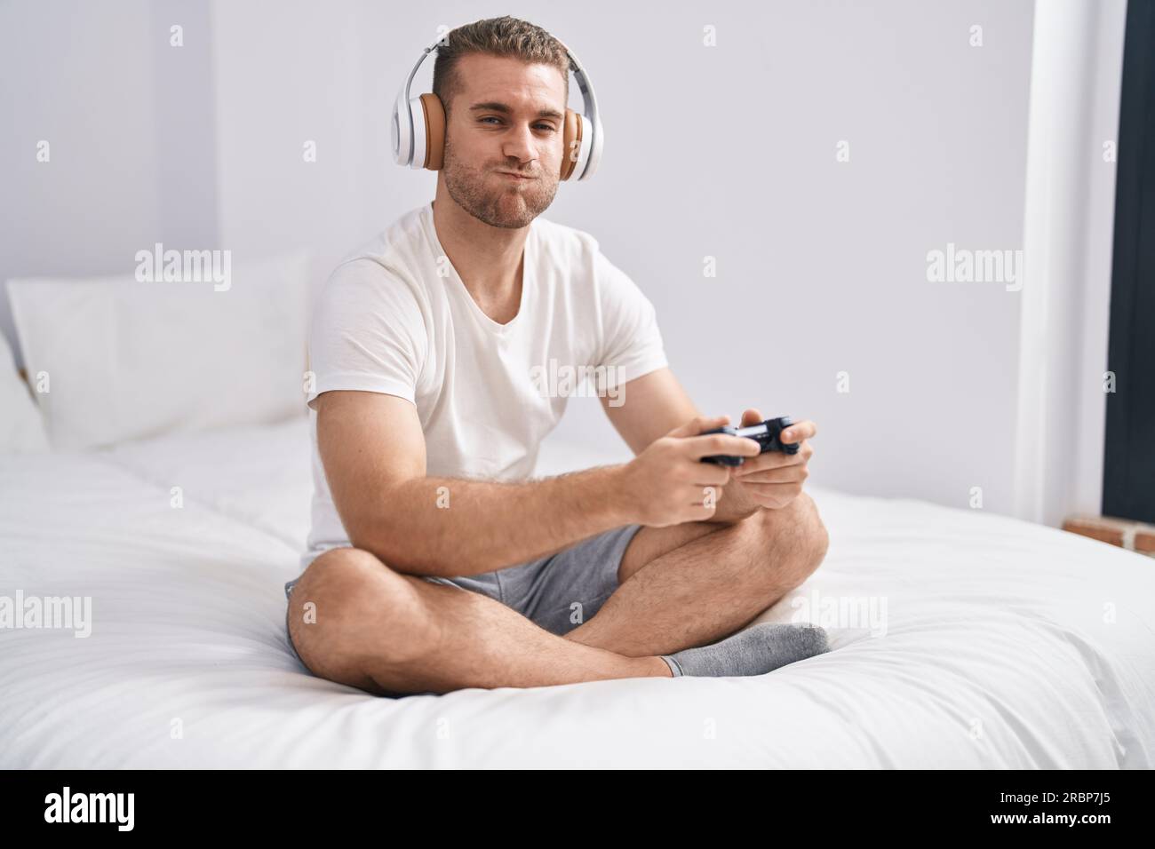 Young caucasian man sitting on the bed at home playing video games ...