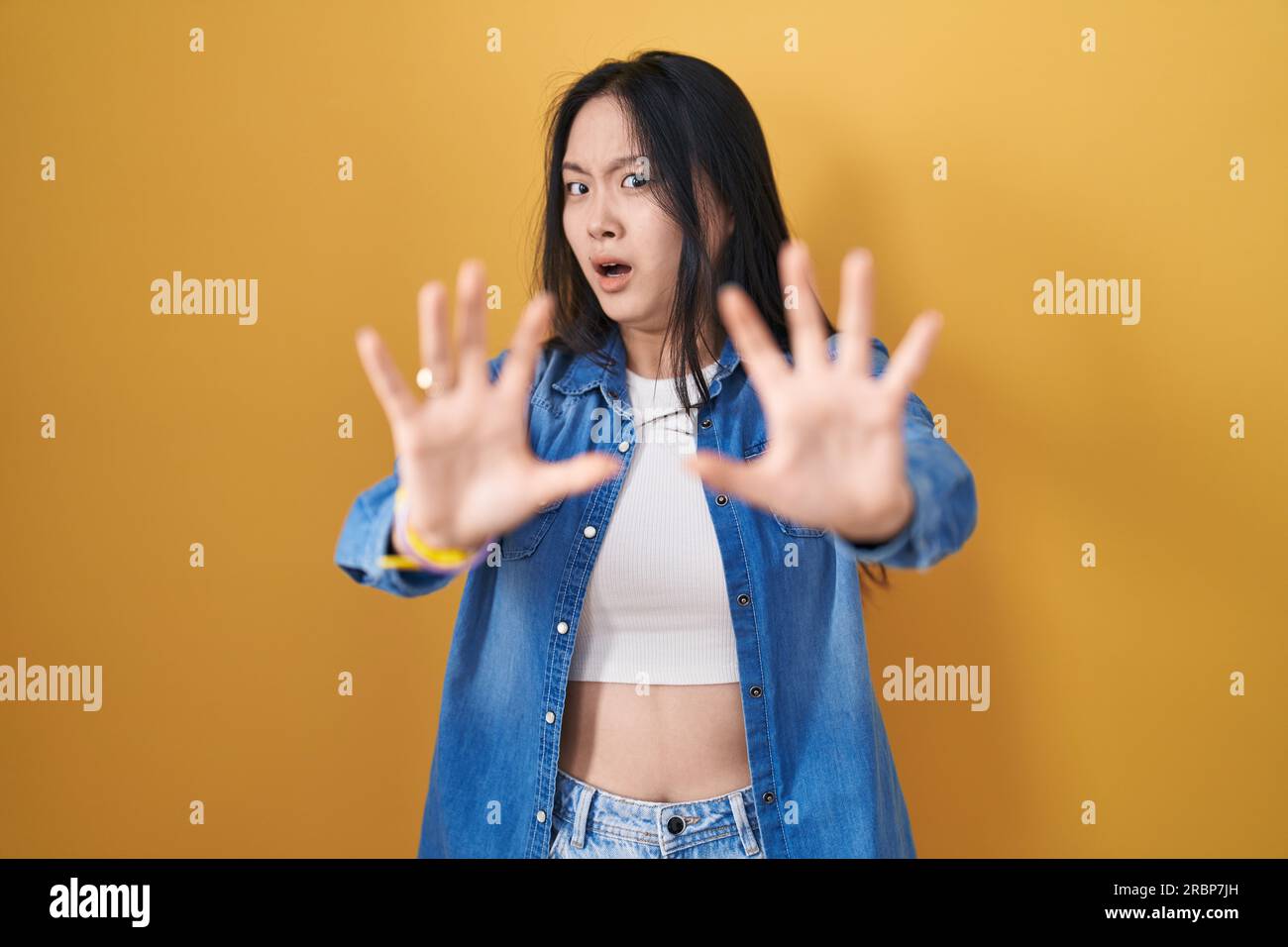 Young asian woman standing over yellow background afraid and terrified ...