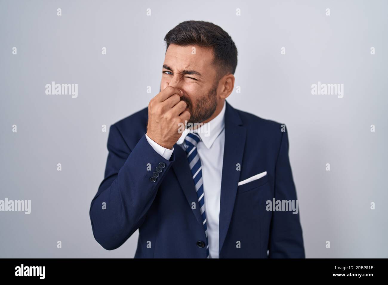 Handsome hispanic man wearing suit and tie smelling something stinky ...