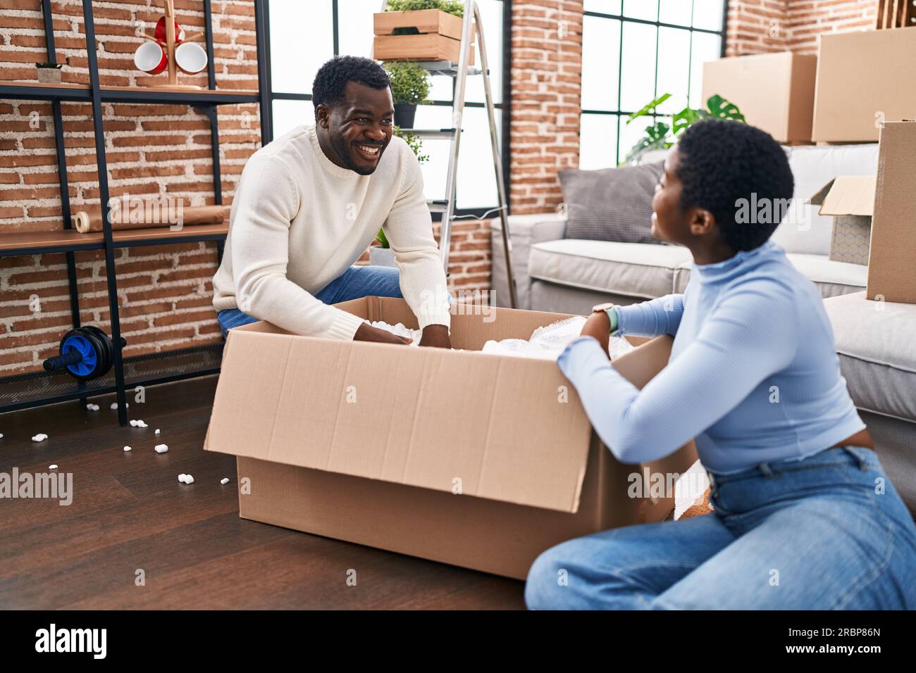 Man And Woman Couple Unboxing Cardboard Box Sitting On Floor At New