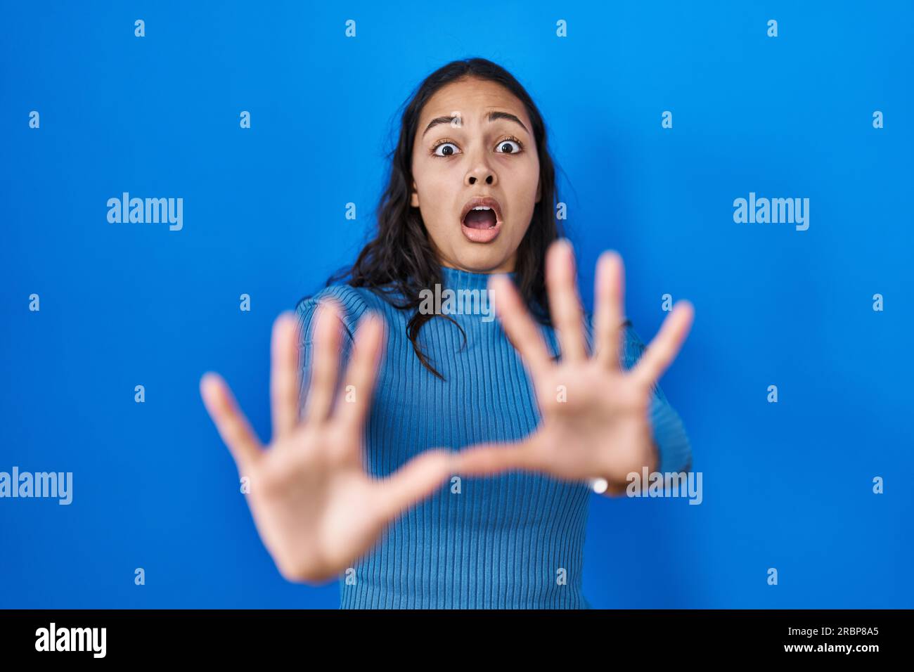 Young brazilian woman standing over blue isolated background afraid and ...