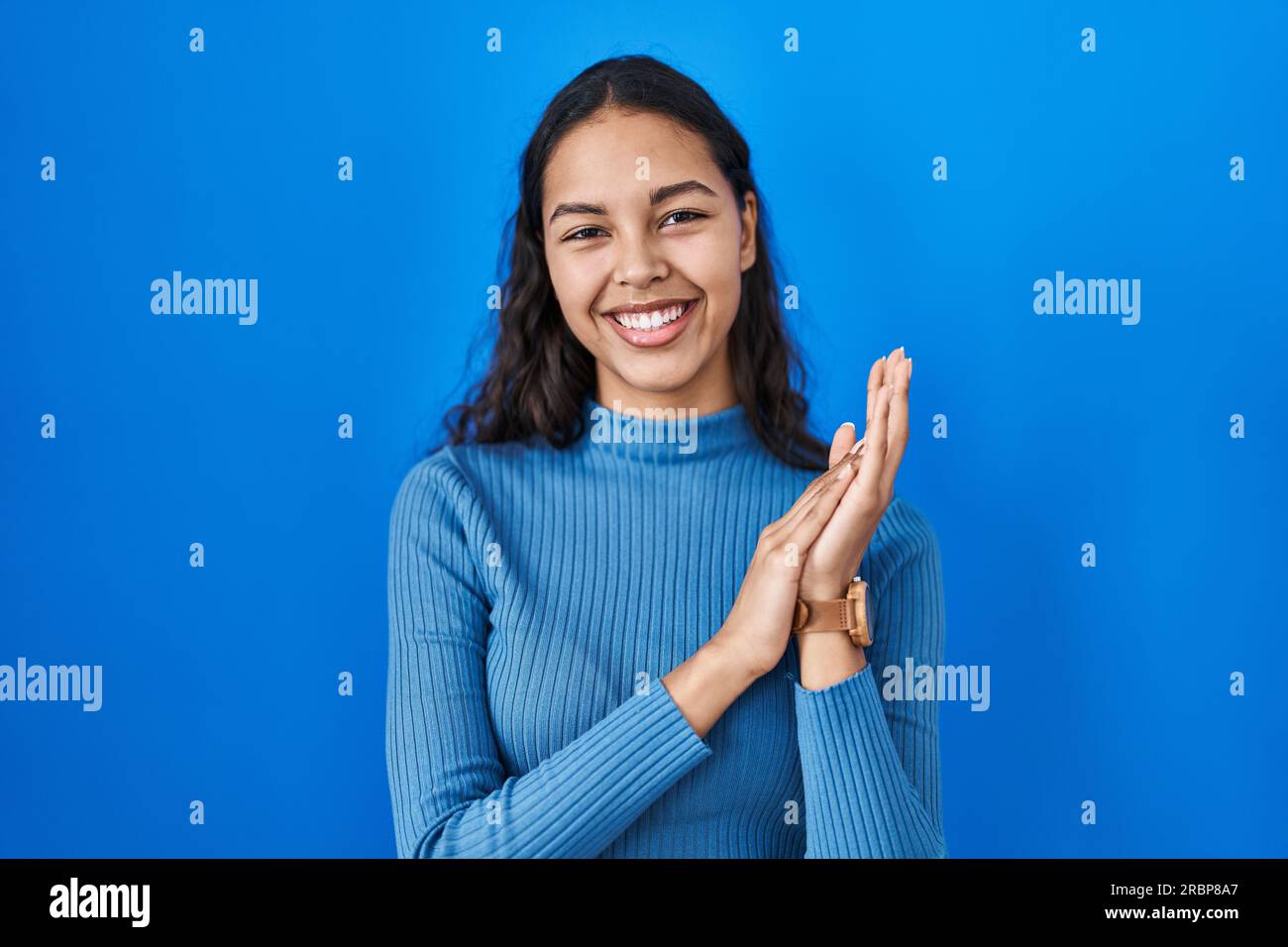 Young brazilian woman standing over blue isolated background clapping ...