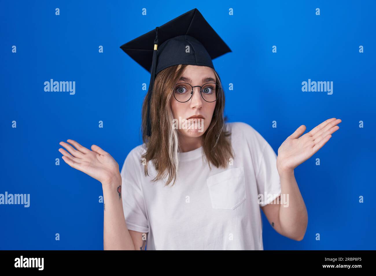 Blonde caucasian woman wearing graduation cap clueless and confused ...