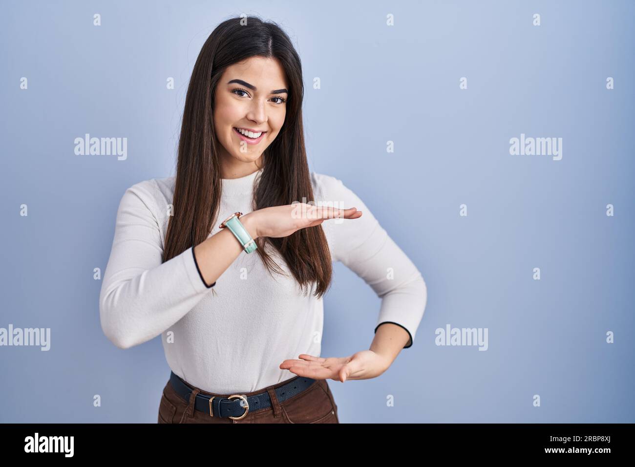 Young brunette woman standing over blue background gesturing with hands ...