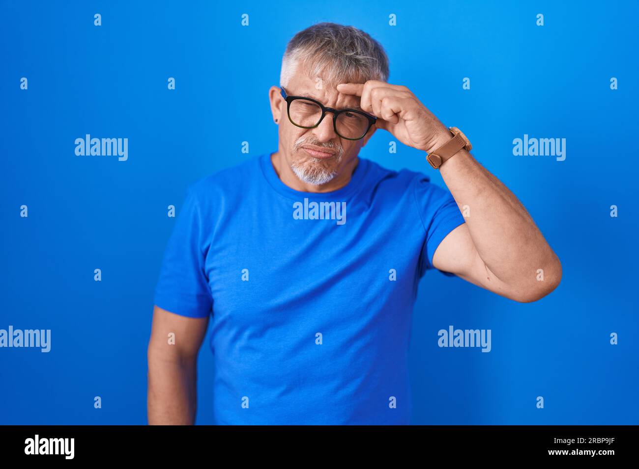 Hispanic man with grey hair standing over blue background pointing ...