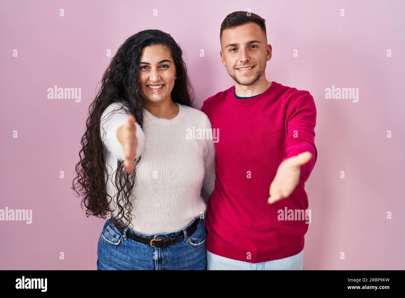 Young hispanic couple standing over pink background smiling friendly ...