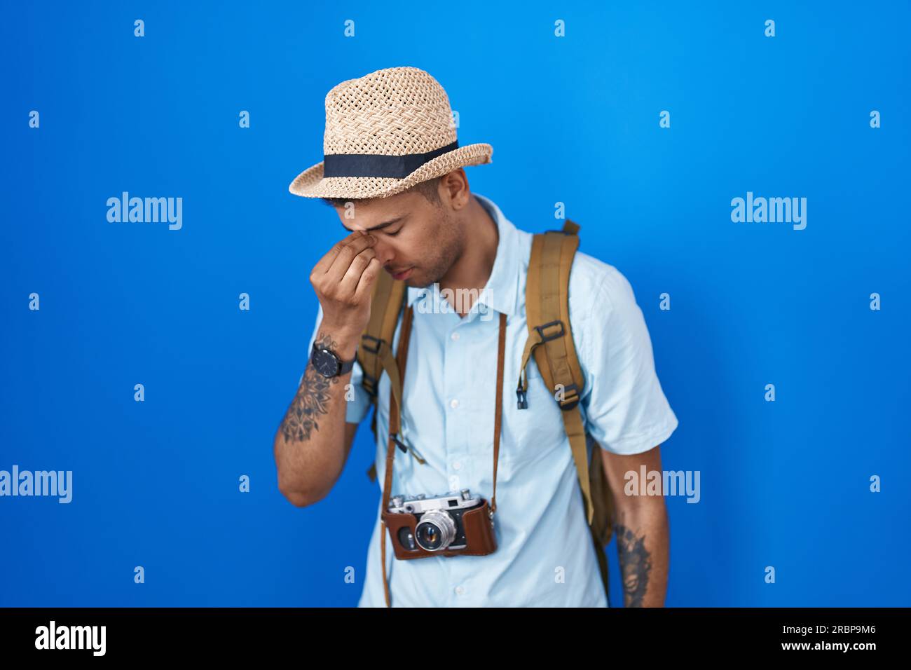 Brazilian young man holding vintage camera tired rubbing nose and eyes ...