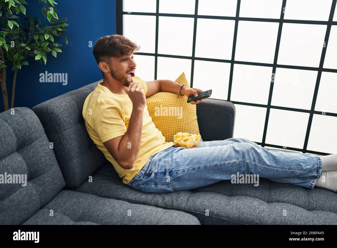 Young arab man eating chips potatoes watching movie at home Stock Photo ...