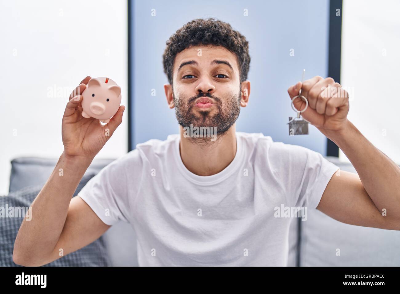 Arab man holding piggy bank and house keys puffing cheeks with funny ...