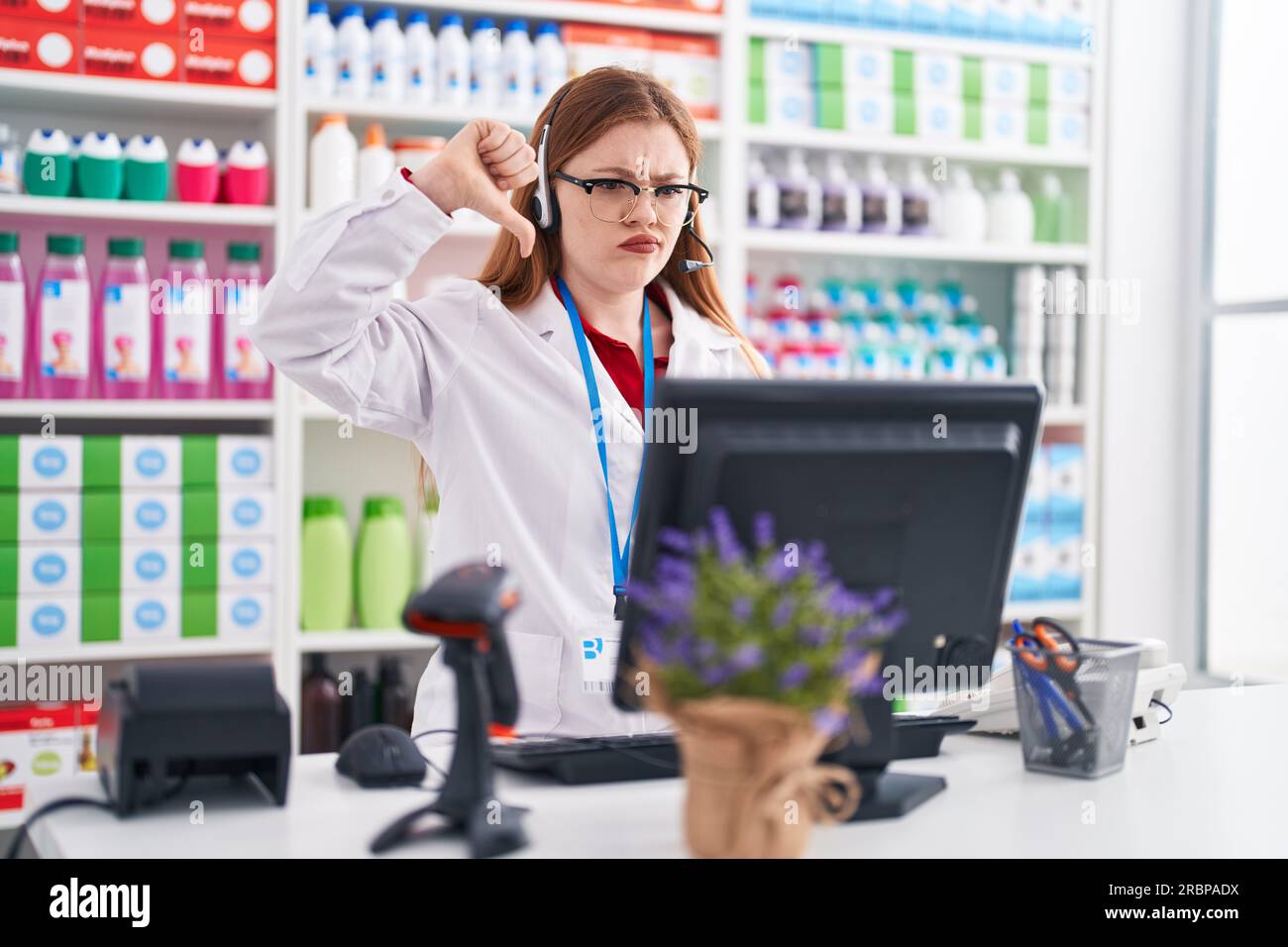 Redhead woman working at pharmacy drugstore wearing headset with angry ...