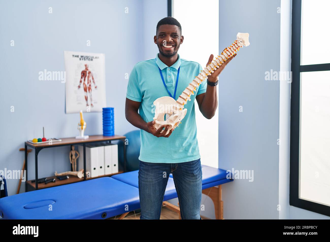 African american man holding anatomical model of spinal column smiling ...