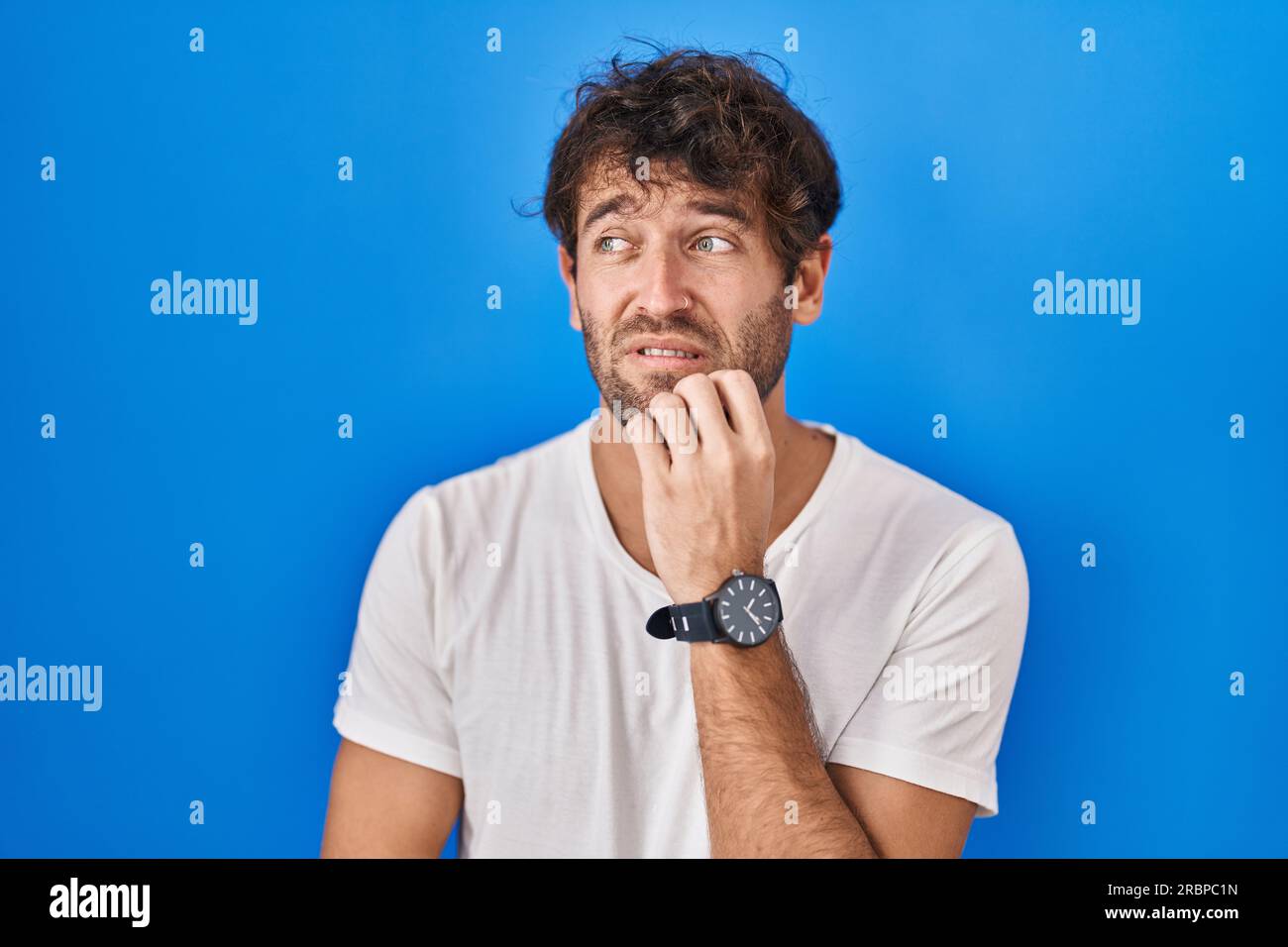 Hispanic young man standing over blue background looking stressed and ...