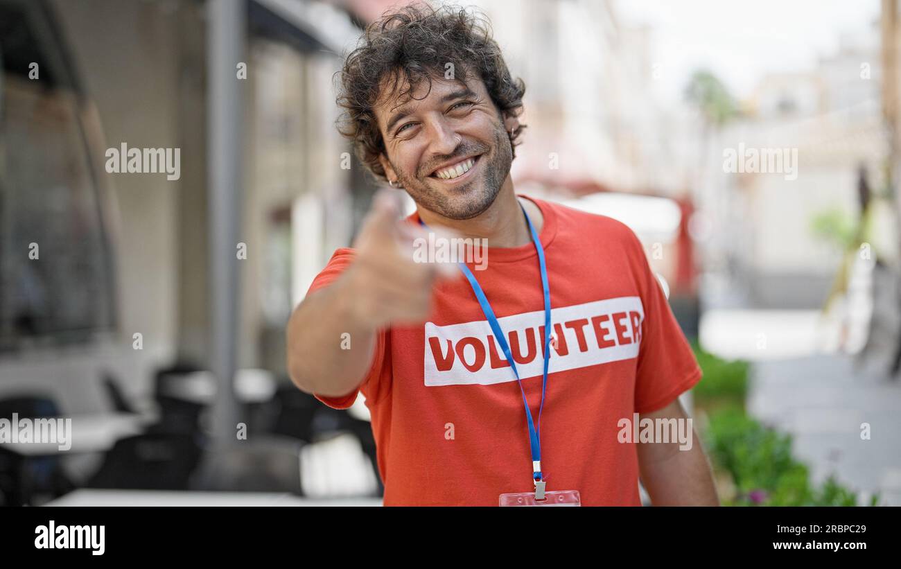 Young hispanic man activist wearing volunteer uniform pointing to ...