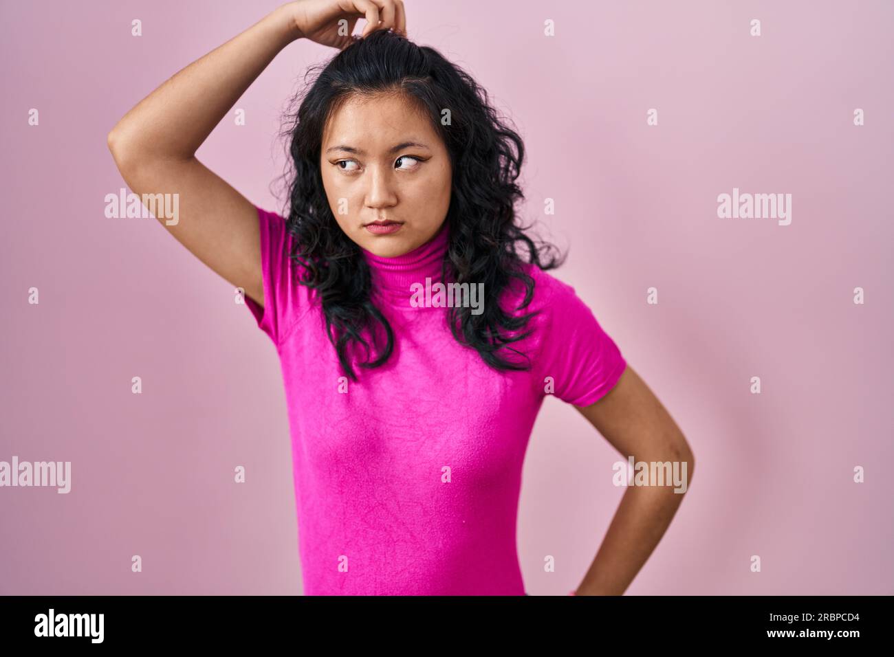 Young asian woman standing over pink background confuse and wondering ...