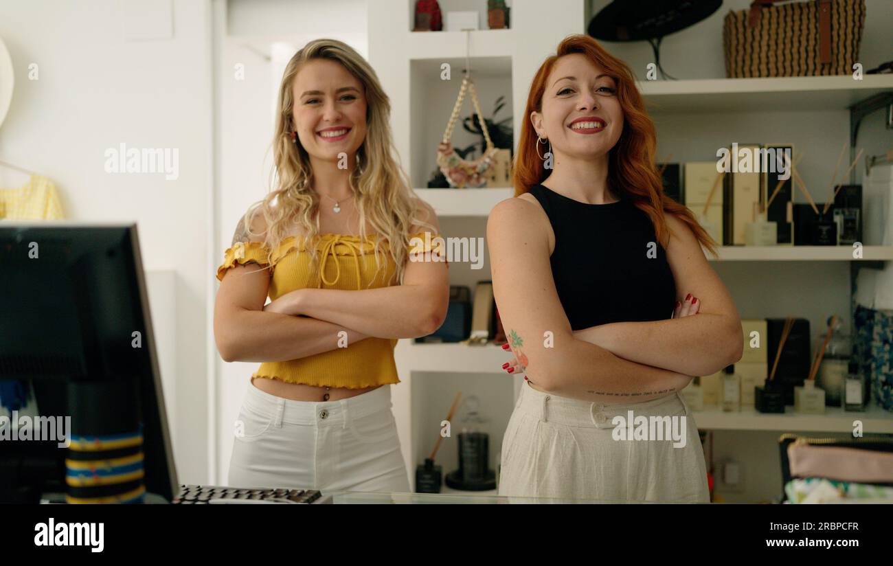 Two women shop employees standing with arms crossed gesture at clothing ...