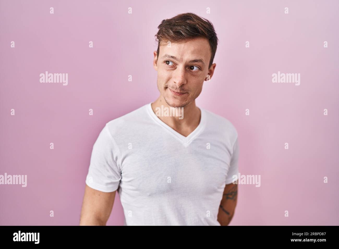Caucasian man standing over pink background smiling looking to the side ...