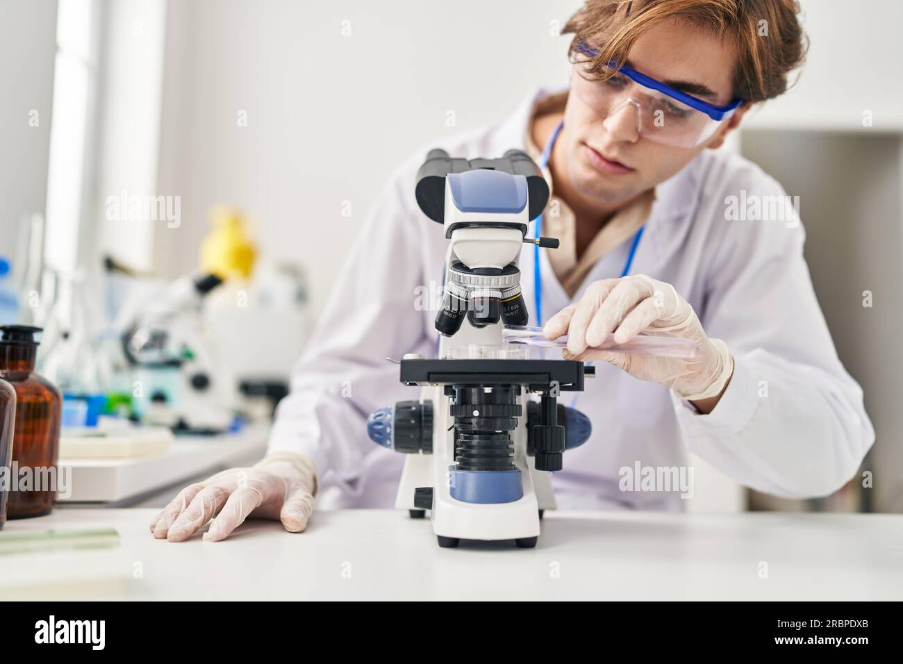 Young caucasian man scientist using microscope pouring liquid on sample ...