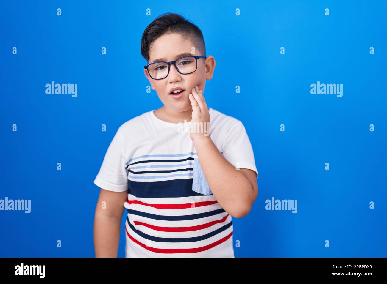 Young hispanic kid standing over blue background touching mouth with ...