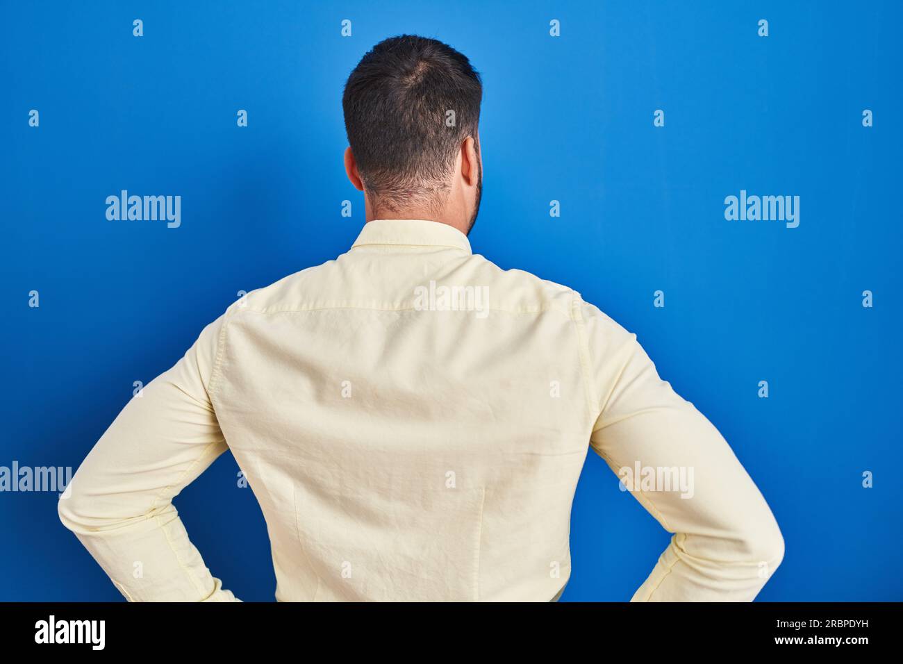 Handsome hispanic man standing over blue background standing backwards ...