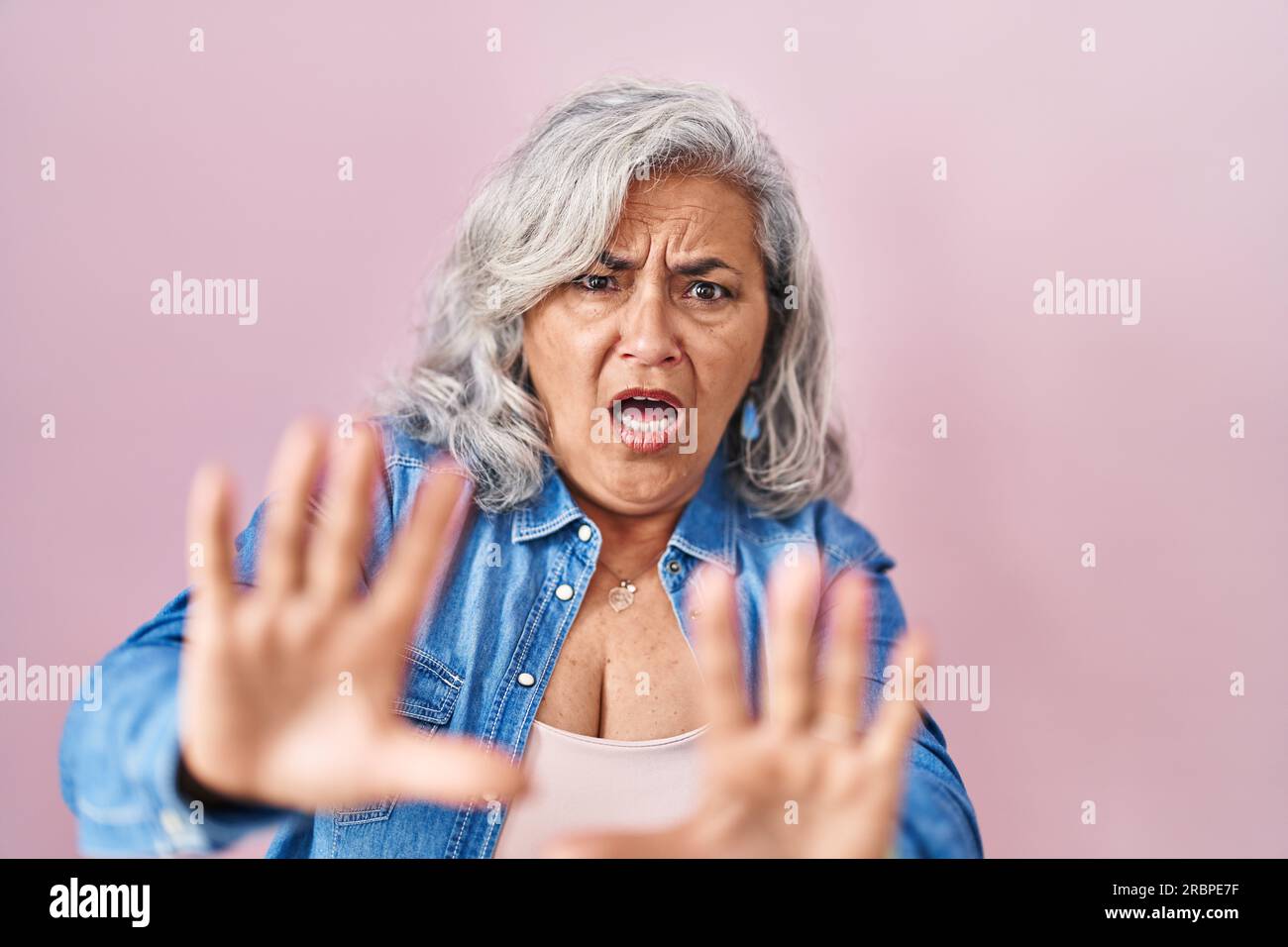 Middle age woman with grey hair standing over pink background afraid ...