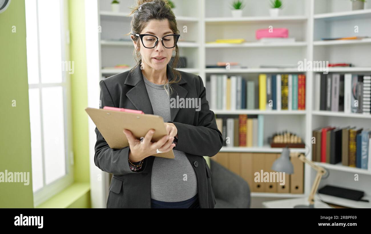 Young pregnant woman teacher reading clipboard explaining lesson at ...