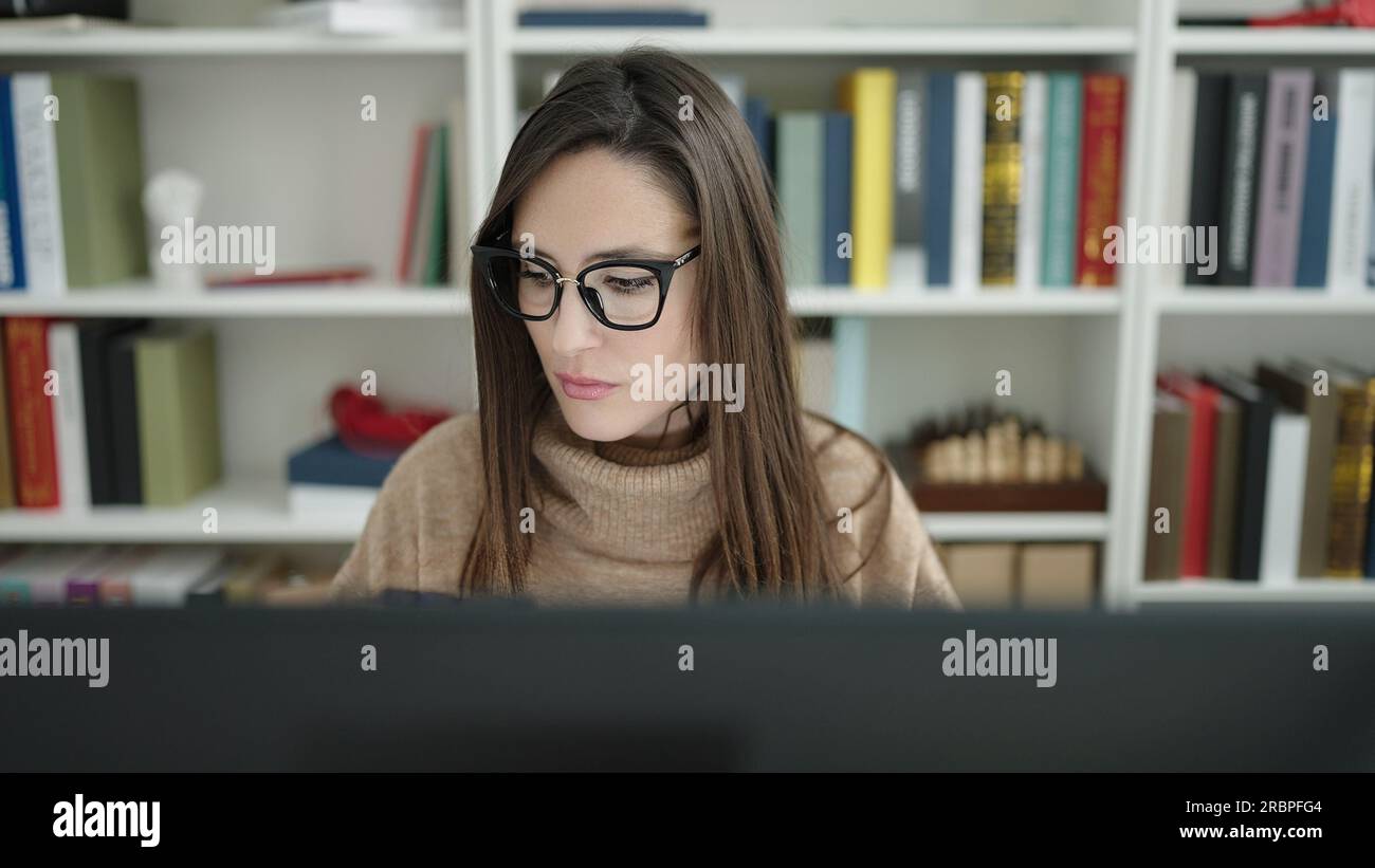 Beautiful hispanic woman student using computer studying at library ...