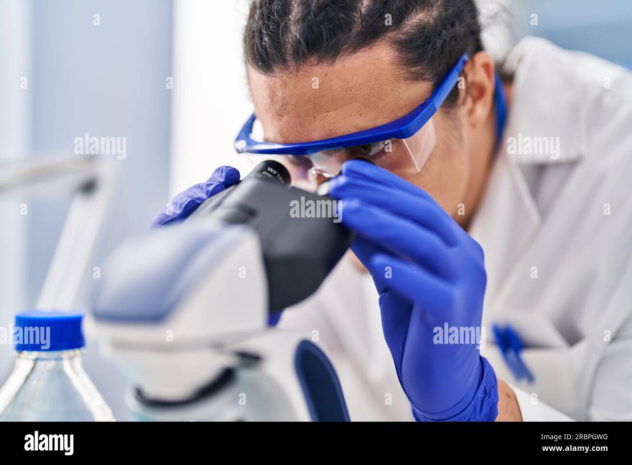 Young man wearing scientist uniform using microscope at laboratory ...