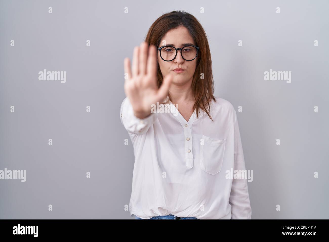 Brunette woman standing over white isolated background doing stop sing ...