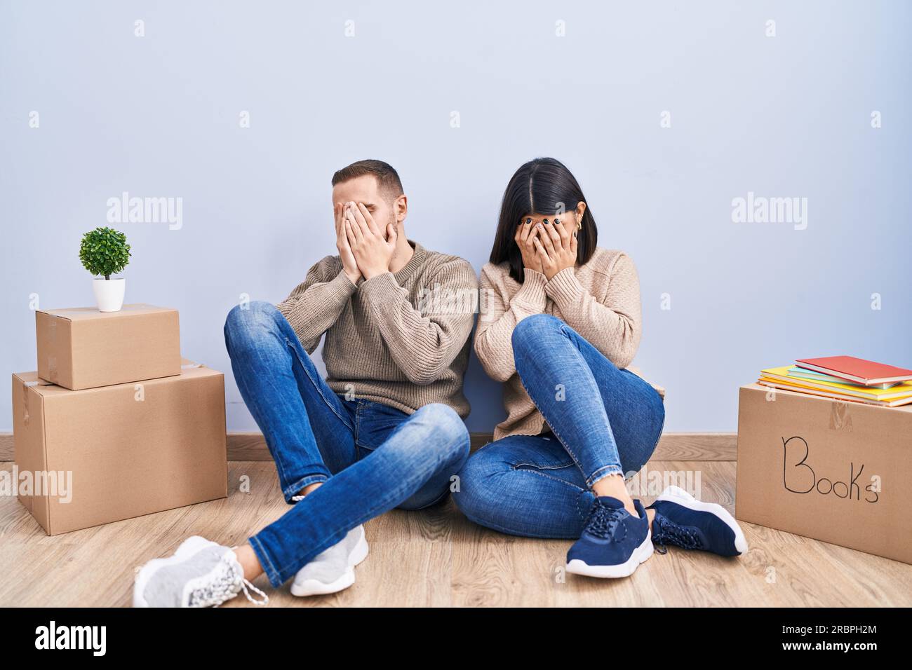 Young couple moving to a new home with sad expression covering face ...