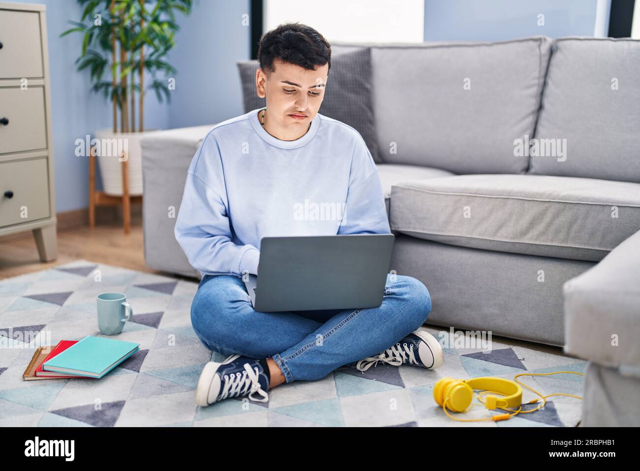 Non binary person studying using computer laptop sitting on the floor ...