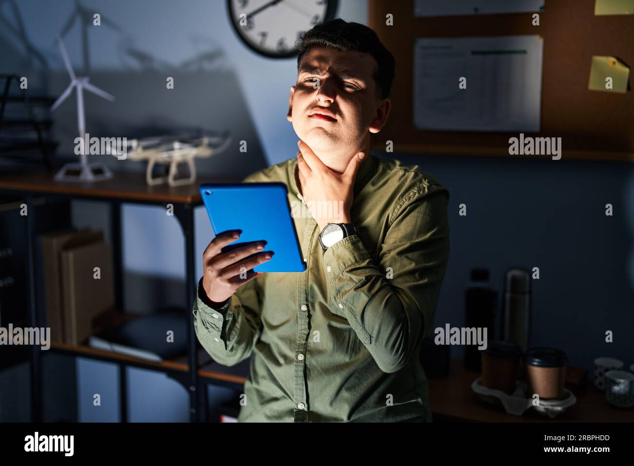 Non binary person using touchpad device at night touching painful neck ...