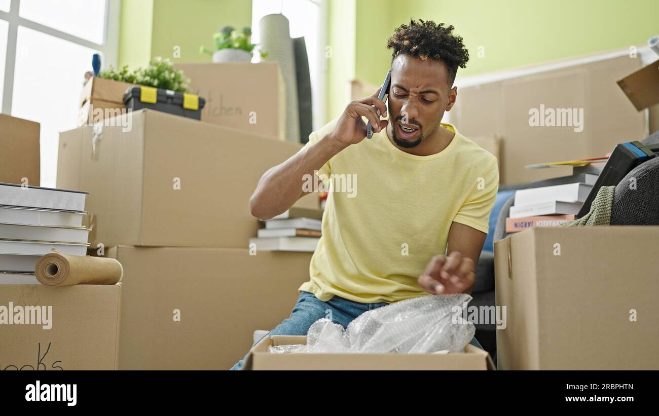 African american man unpacking cardboard box talking on smartphone ...