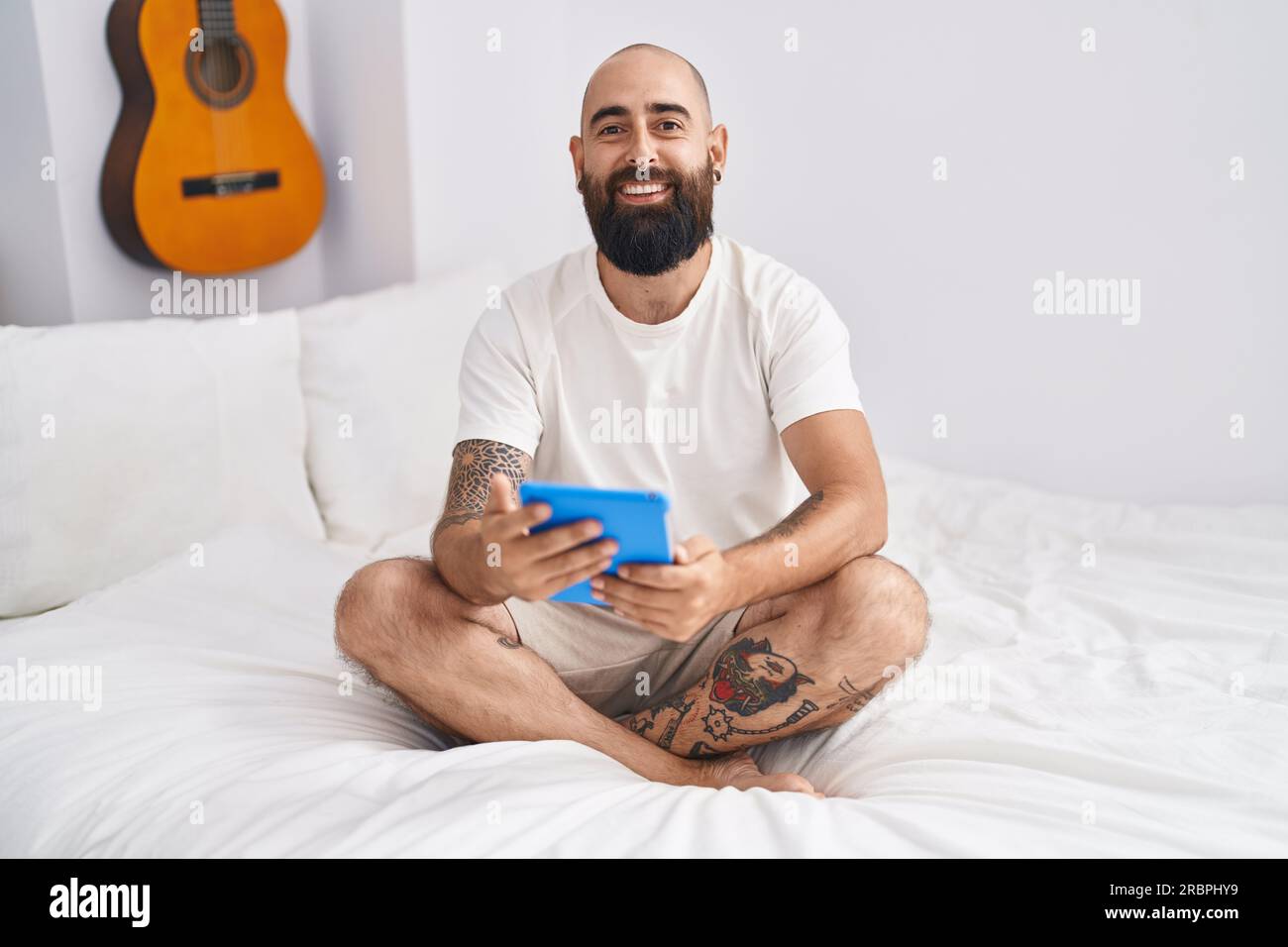 Young bald man using touchpad sitting on bed at bedroom Stock Photo - Alamy