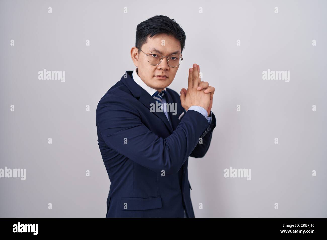 Young asian man wearing business suit and tie holding symbolic gun with ...