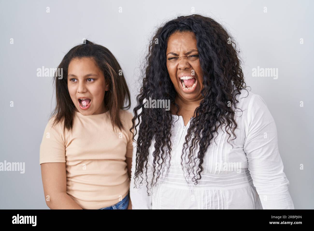Mother and young daughter standing over white background angry and mad ...