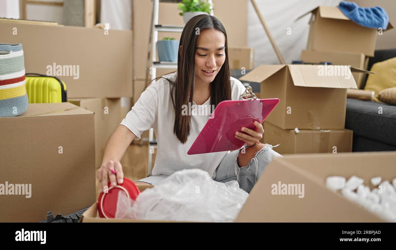 Young beautiful hispanic woman unpacking cardboard box checking on ...