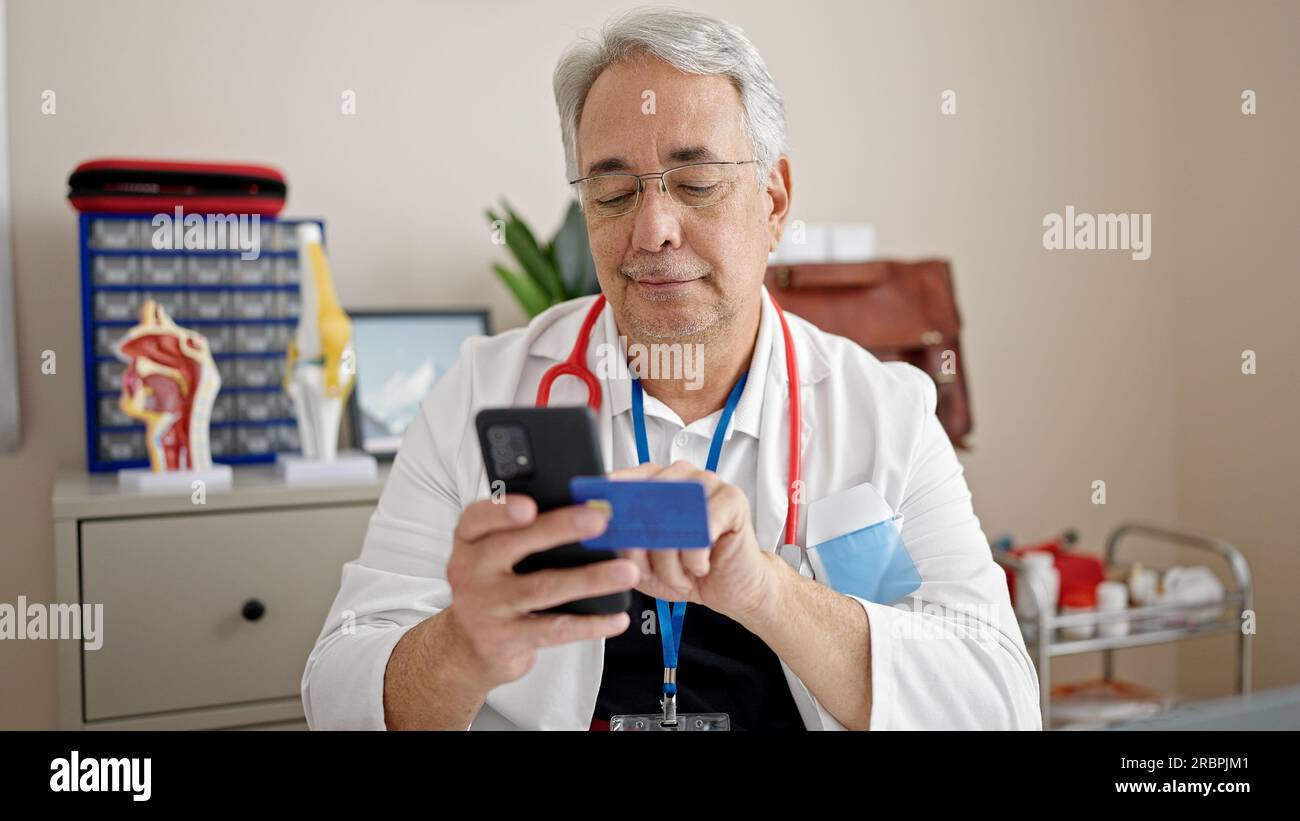 Middle age man with grey hair doctor using smartphone working doing ...