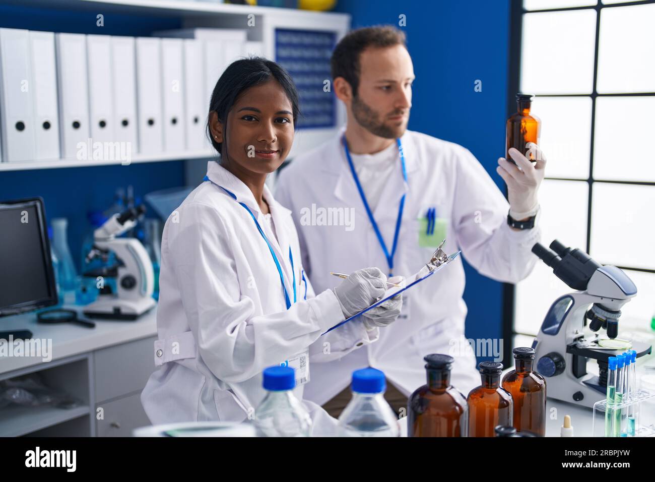Man and woman scientists holding bottle writing report at laboratory ...