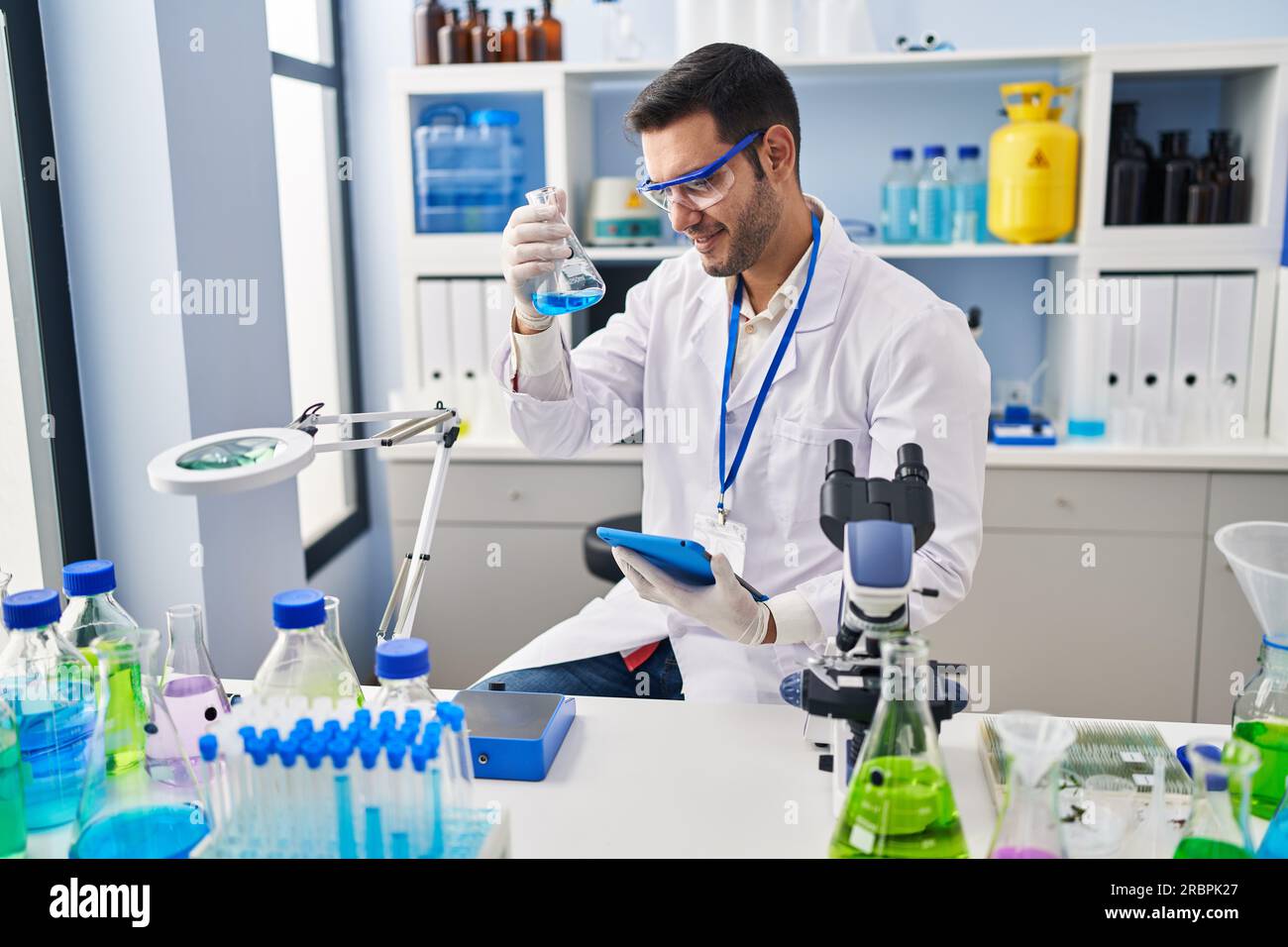 Young hispanic man scientist measuring liquid using touchpad at ...