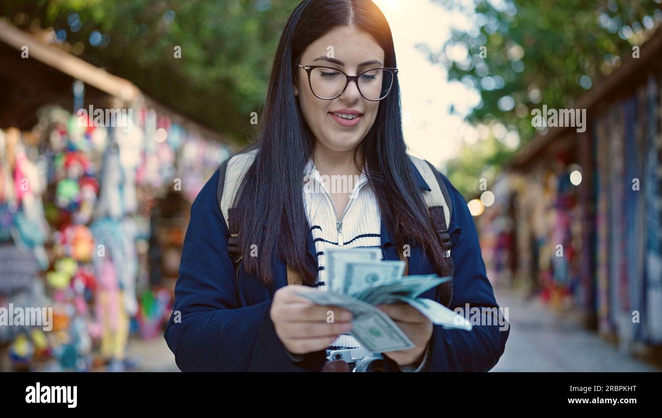Young hispanic woman tourist wearing backpack counting money at street ...