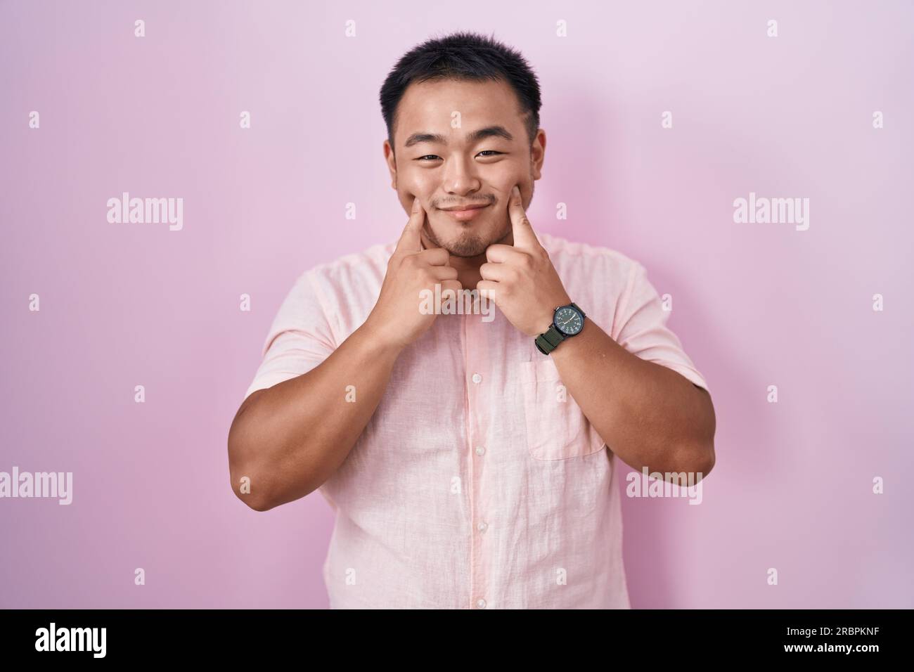 Chinese young man standing over pink background smiling with open mouth ...
