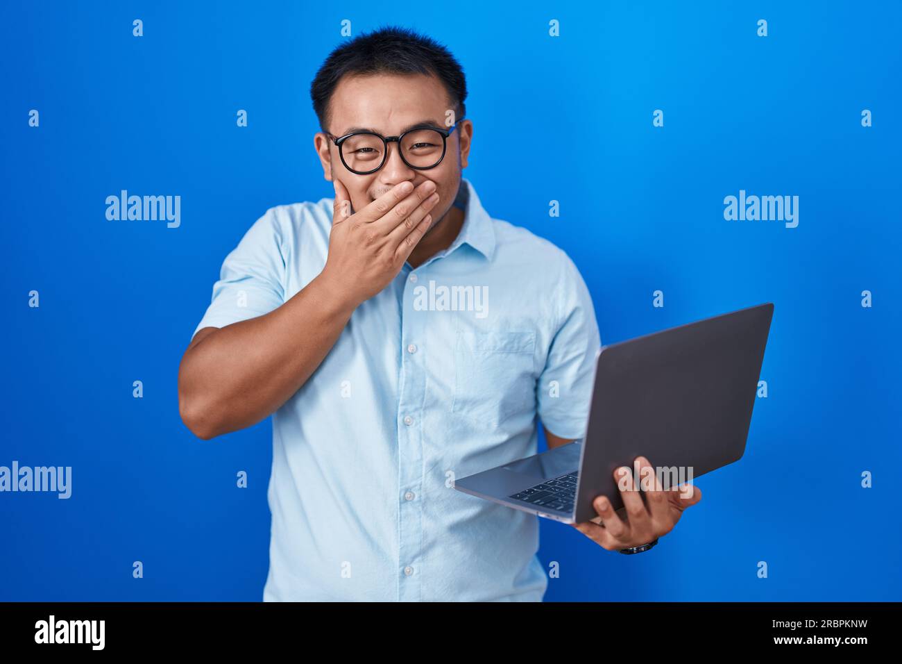 Chinese young man using computer laptop laughing and embarrassed giggle ...