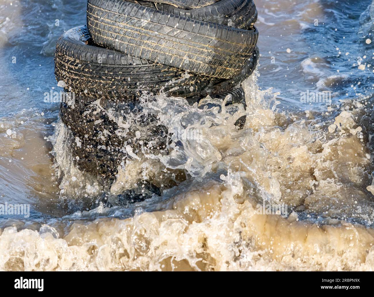 Water waves crash into a coastal barrier made of old tires Stock Photo ...