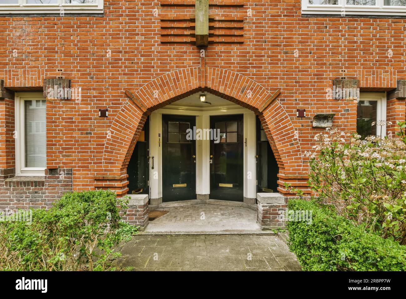 a brick building with an arched door in the middle and green bushes to ...
