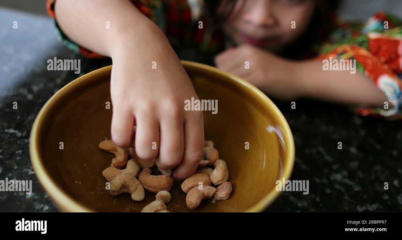 Little girl grabbing cashew nuts from bowl kid eating healthy snack ...