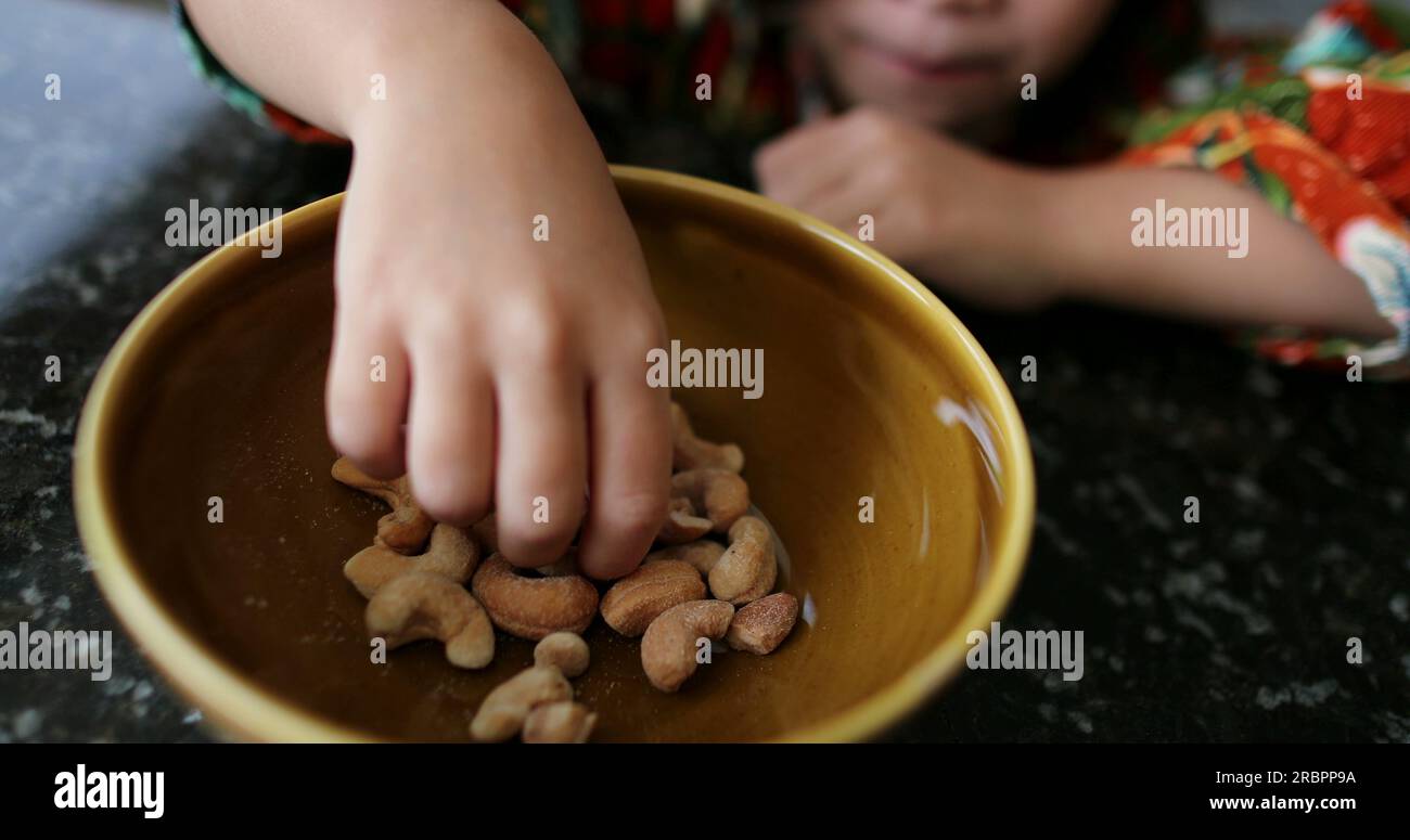 Little girl grabbing cashew nuts from bowl kid eating healthy snack ...