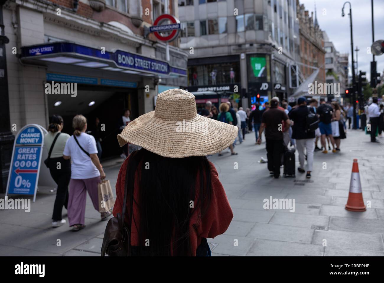 Woman wearing straw summer hat walking long Oxford Street past Bond ...