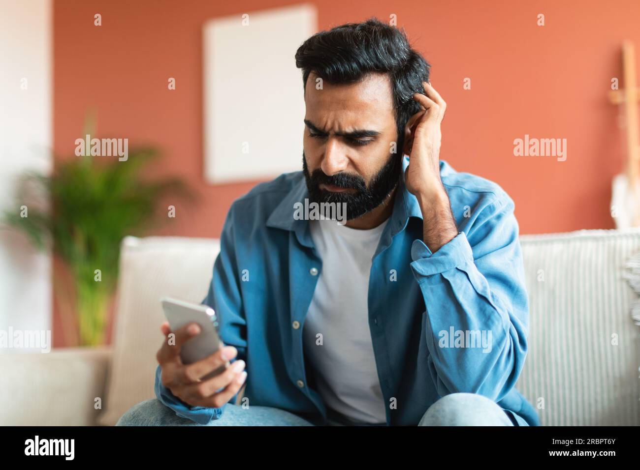 Confused arabic guy looking at smartphone touching head at home Stock ...